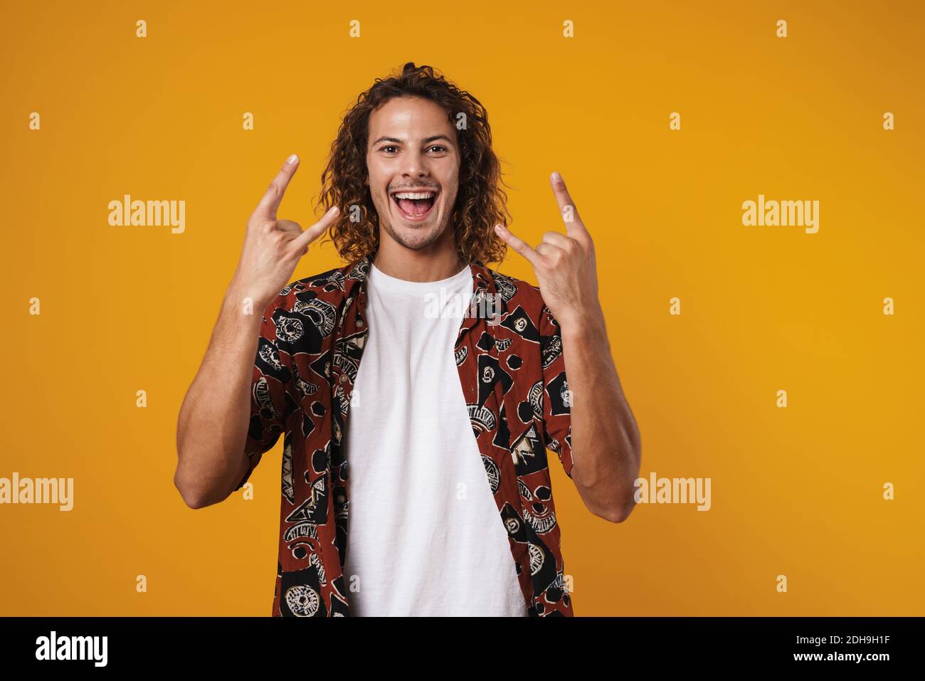 Portrait of a cheerful young man in shirt showing horns up gesture ...