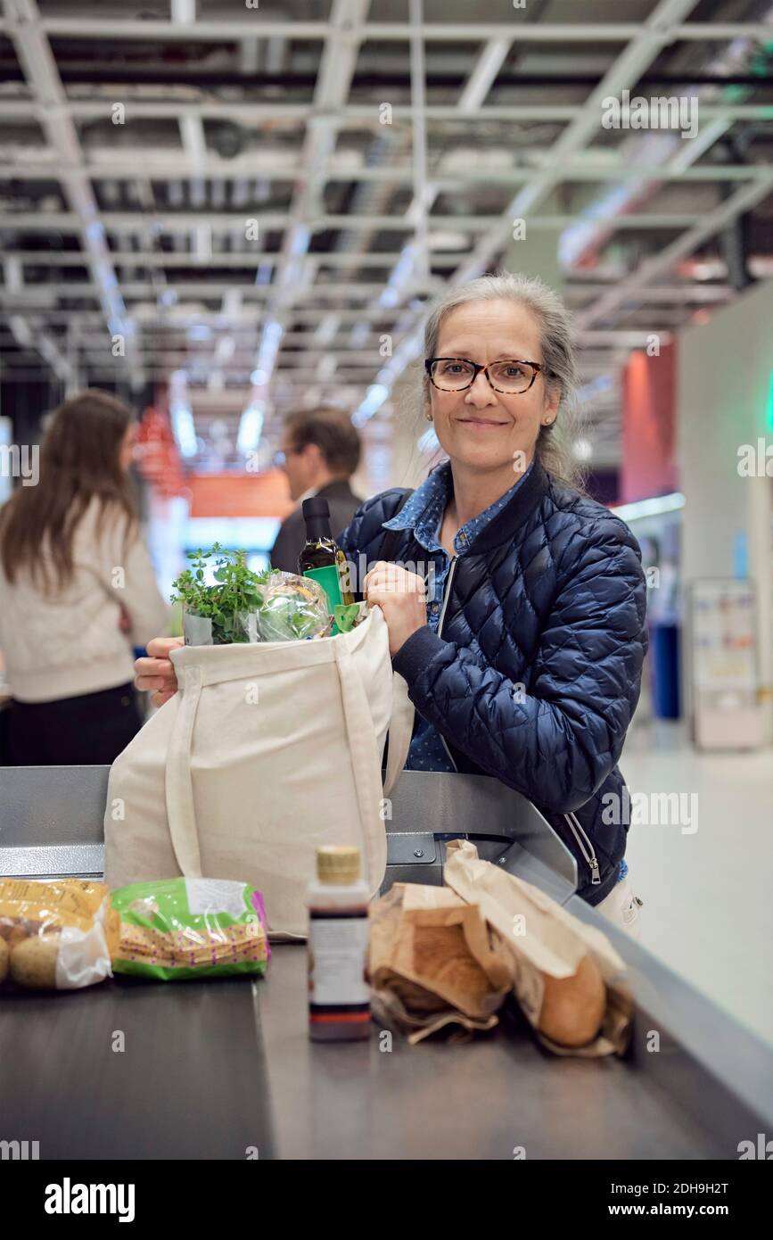 Portrait of woman holding groceries bag at checkout counter in ...
