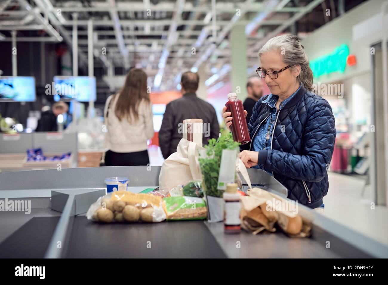 Mature woman keeping juice bottle in bag while standing at checkout ...