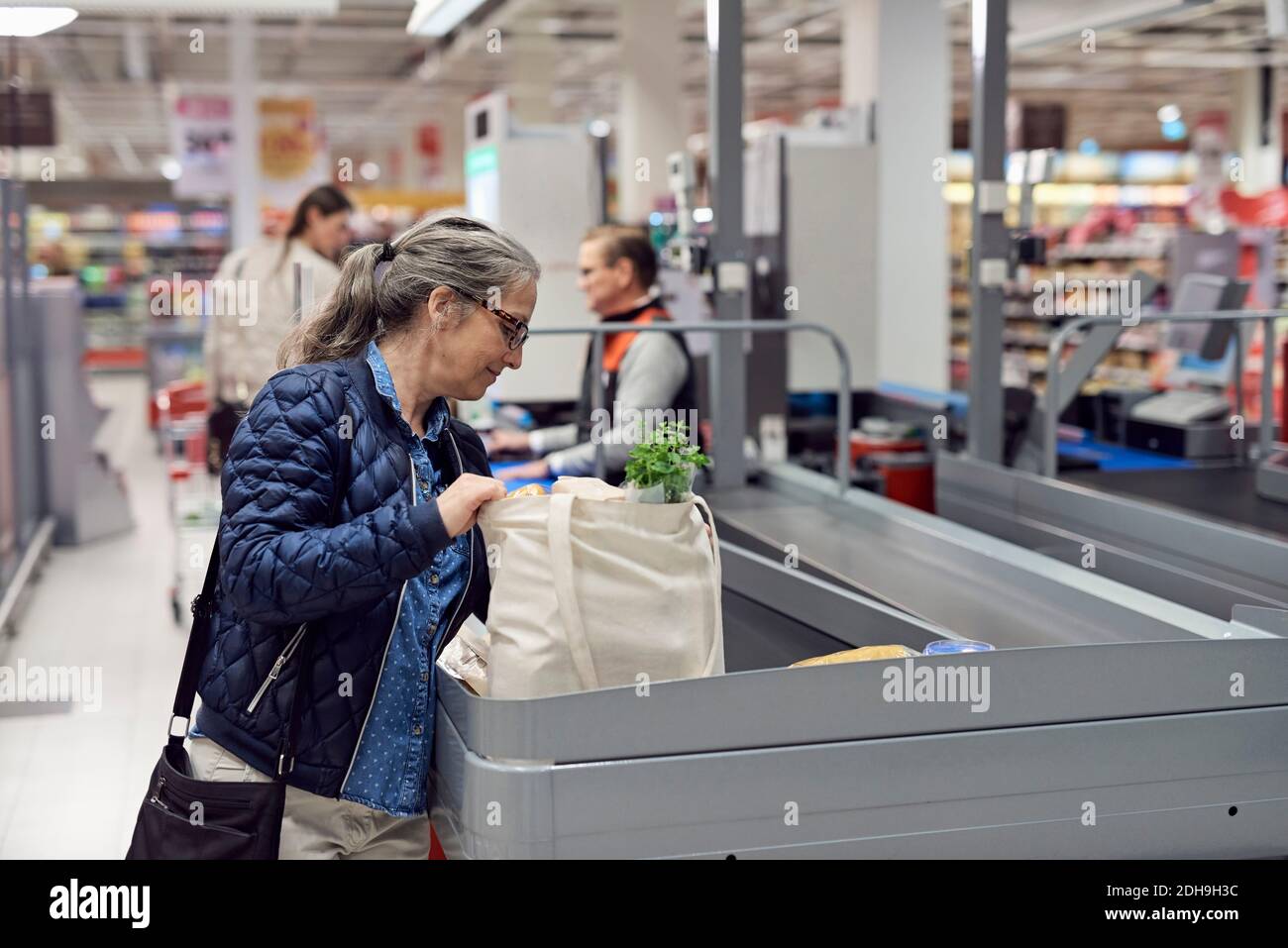 Smiling mature woman holding bag at checkout counter in supermarket ...