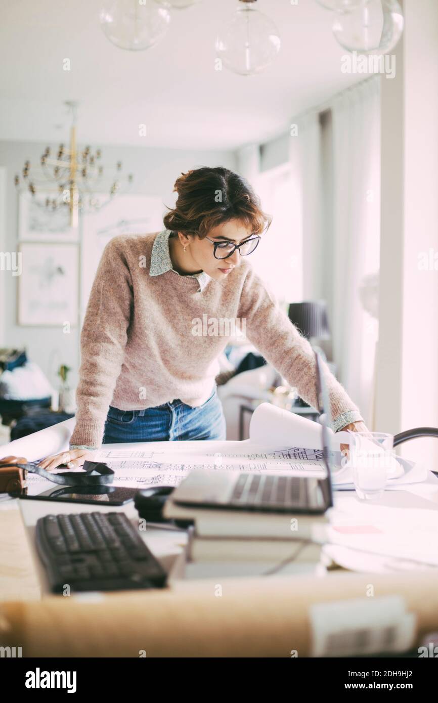Architect standing at table reading blueprint in office at home Stock ...