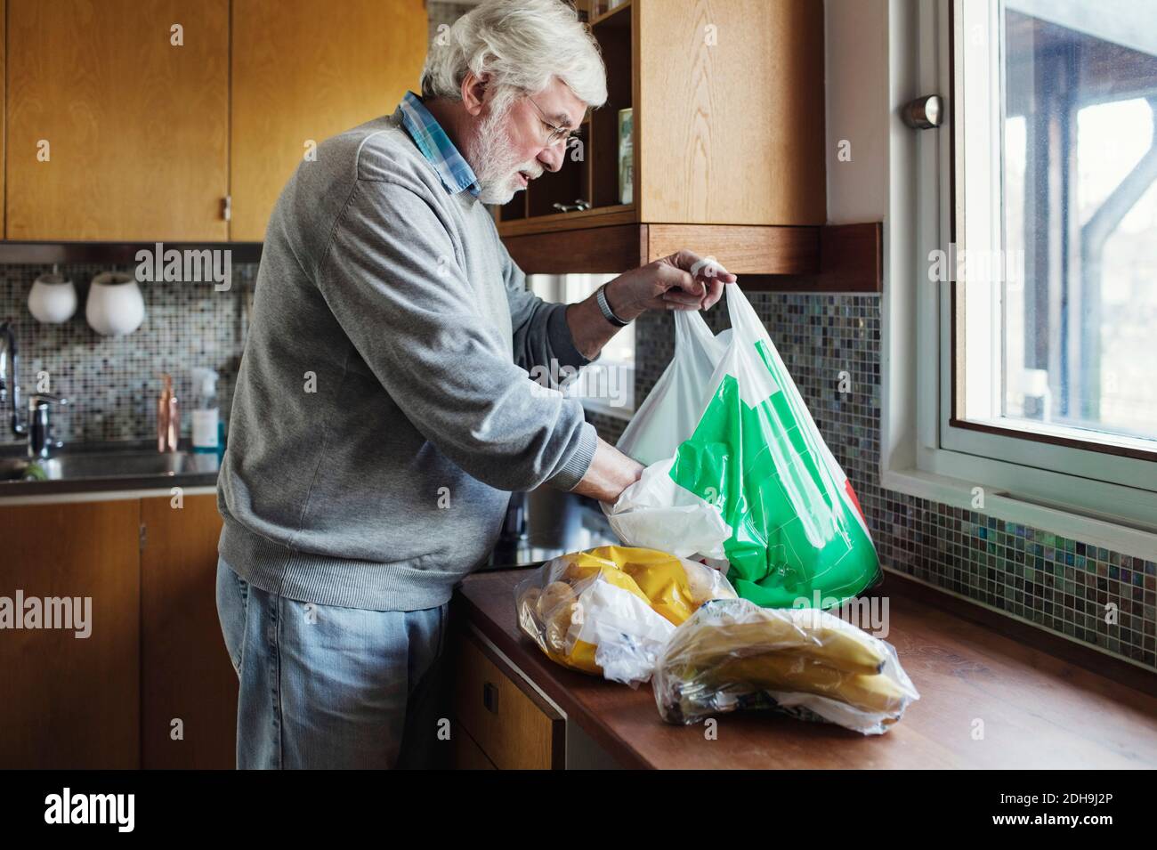 Senior man removing packets from plastic bag at kitchen counter Stock ...
