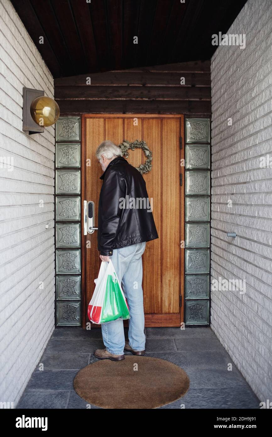 Rear view of man carrying bag opening door Stock Photo - Alamy