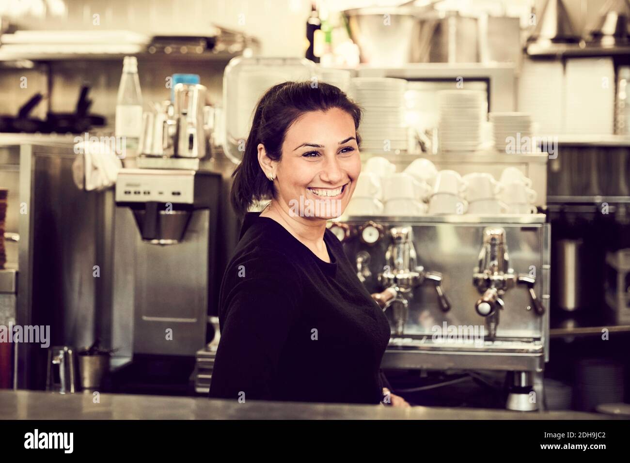 Side view of smiling owner looking away while standing at checkout ...