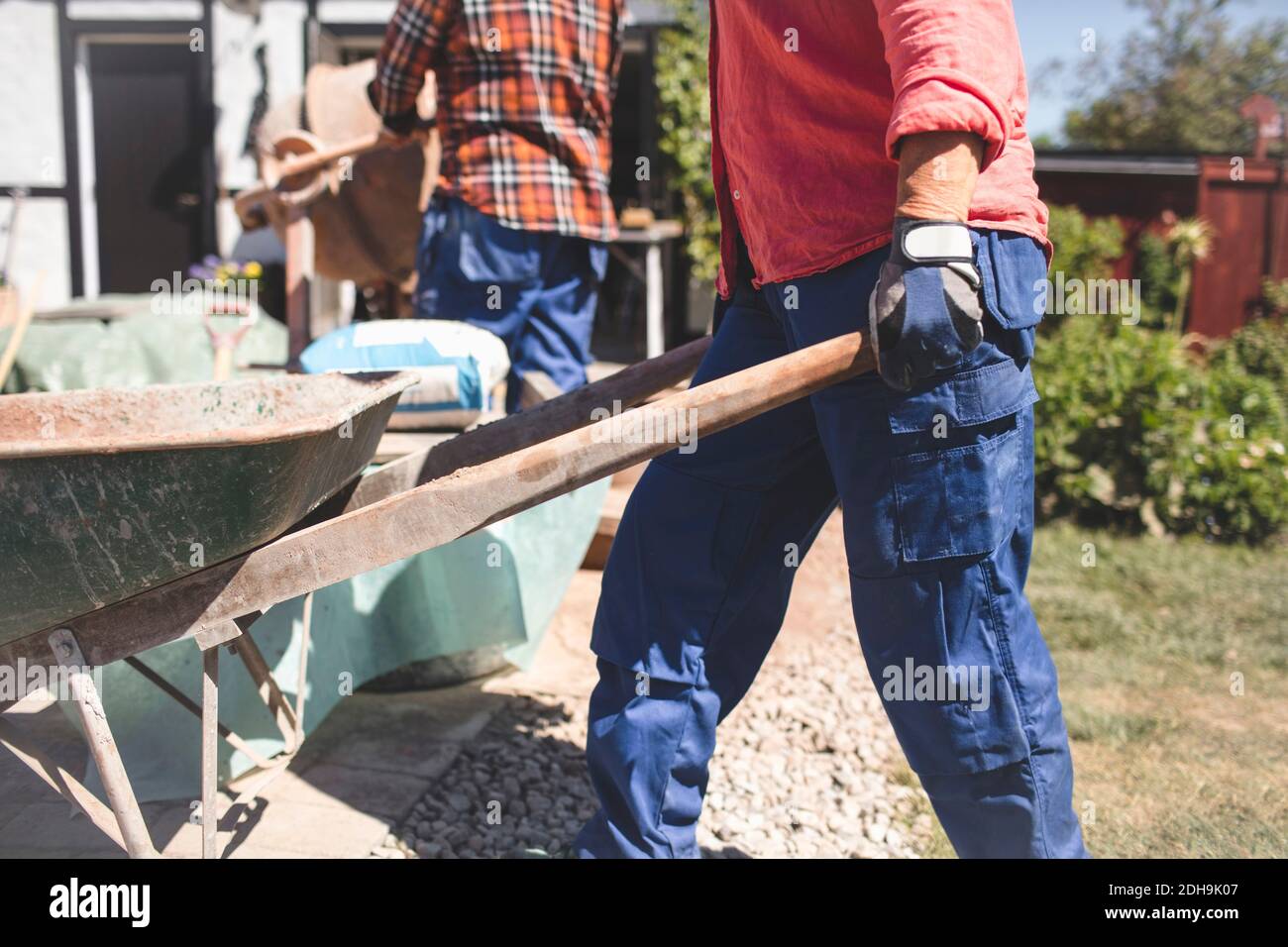 Side view of senior woman pushing wheelbarrow at yard while man ...