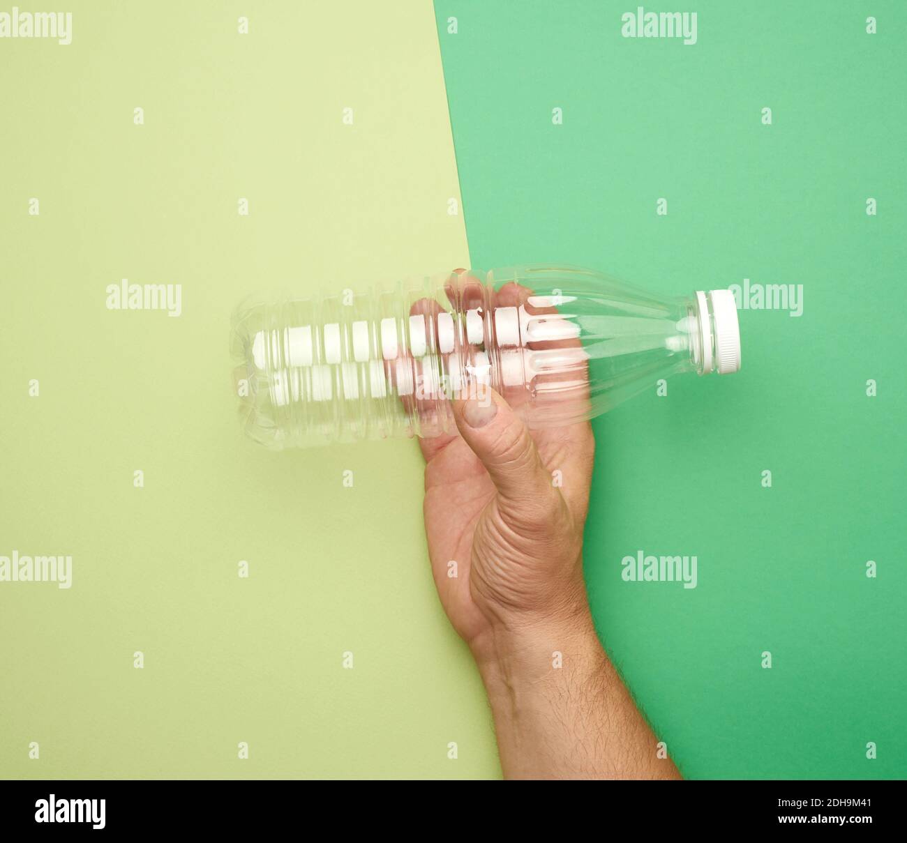Male hand holding empty transparent plastic bottle on green background ...