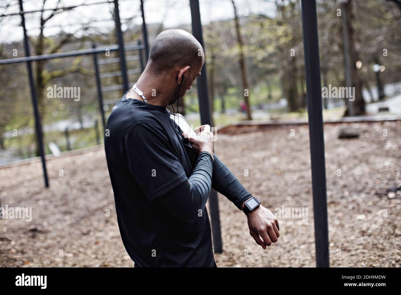 Side view of male athlete using smart phone in arm band at forest Stock ...