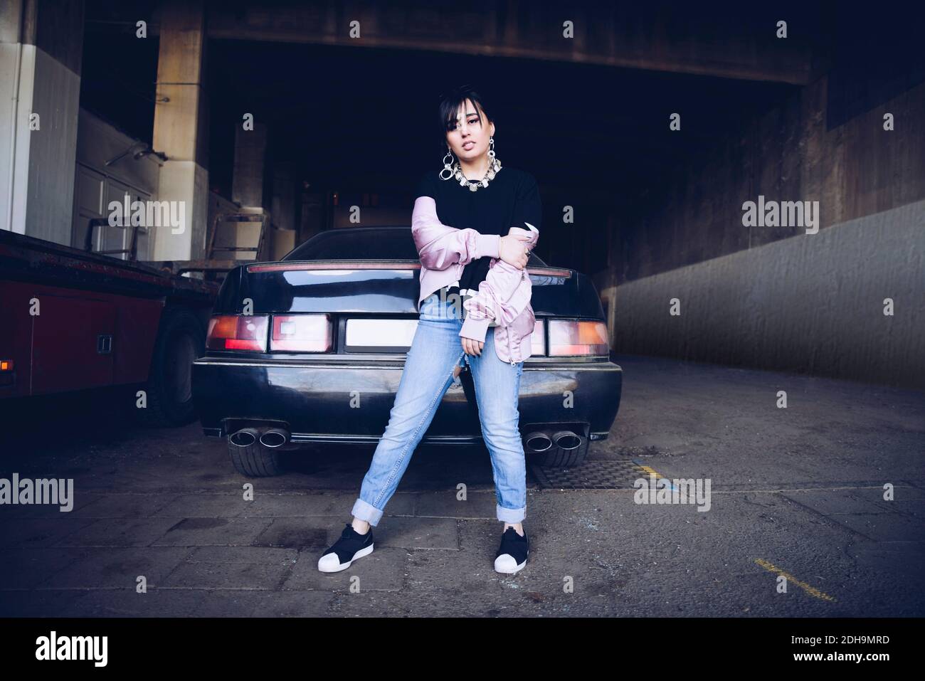 Portrait of young woman standing against car in parking lot Stock Photo ...
