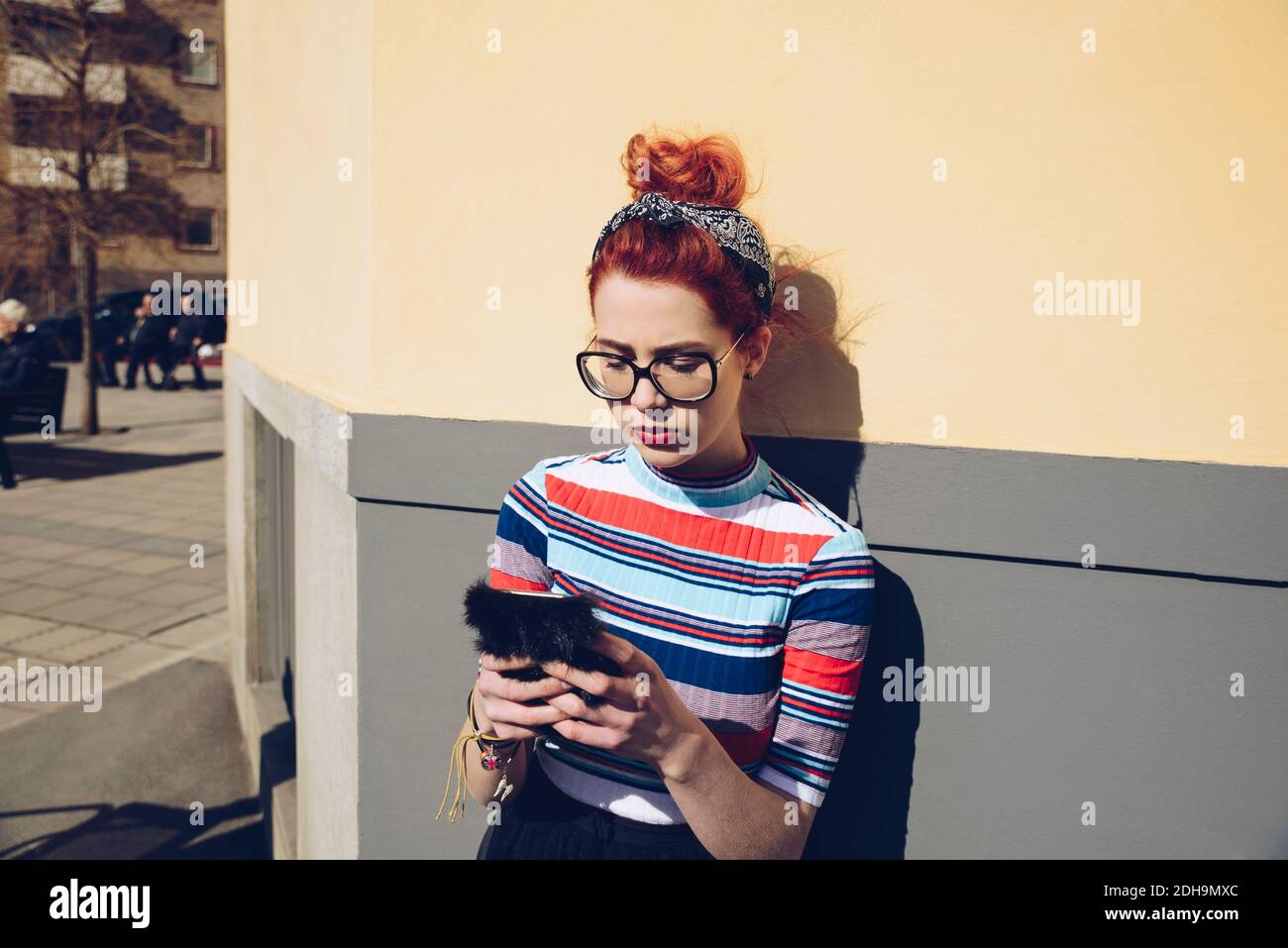 Young woman using mobile phone while standing against wall Stock Photo ...