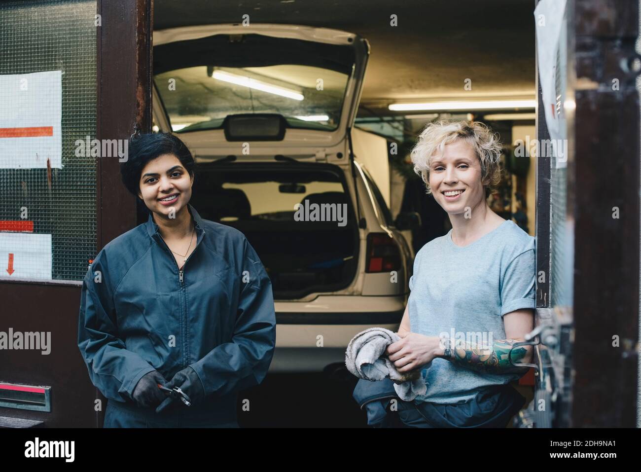 Portrait of female coworkers standing at entrance of auto repair shop ...