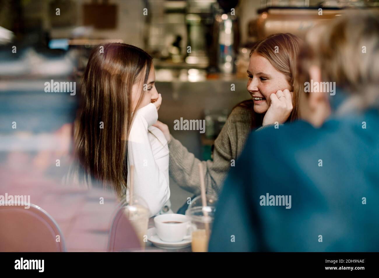 Smiling teenage female friends talking while sitting at cafe seen ...