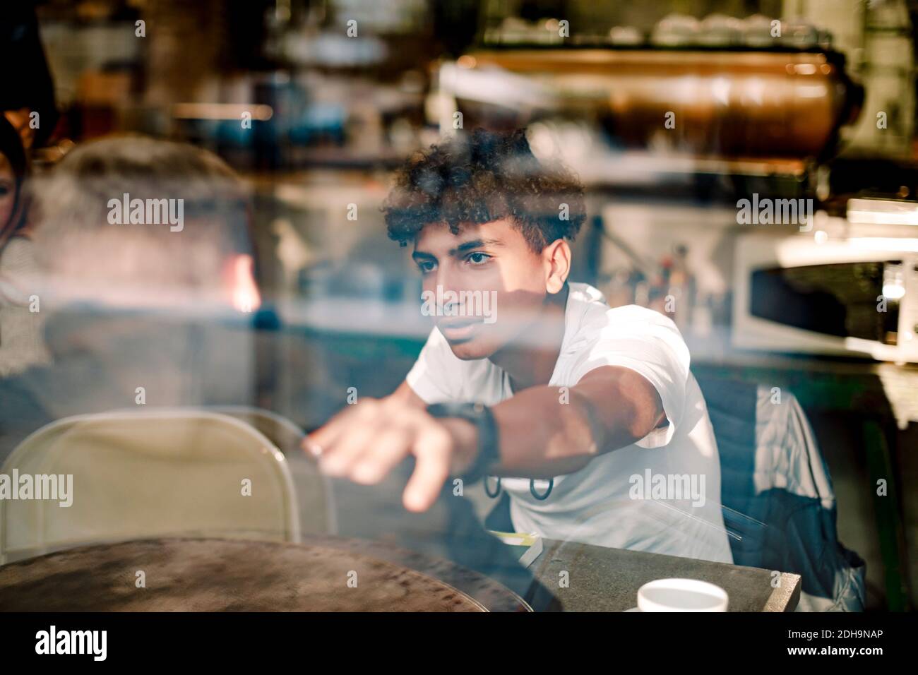 Teenage boy consoling his friend while sitting at cafe seen through ...