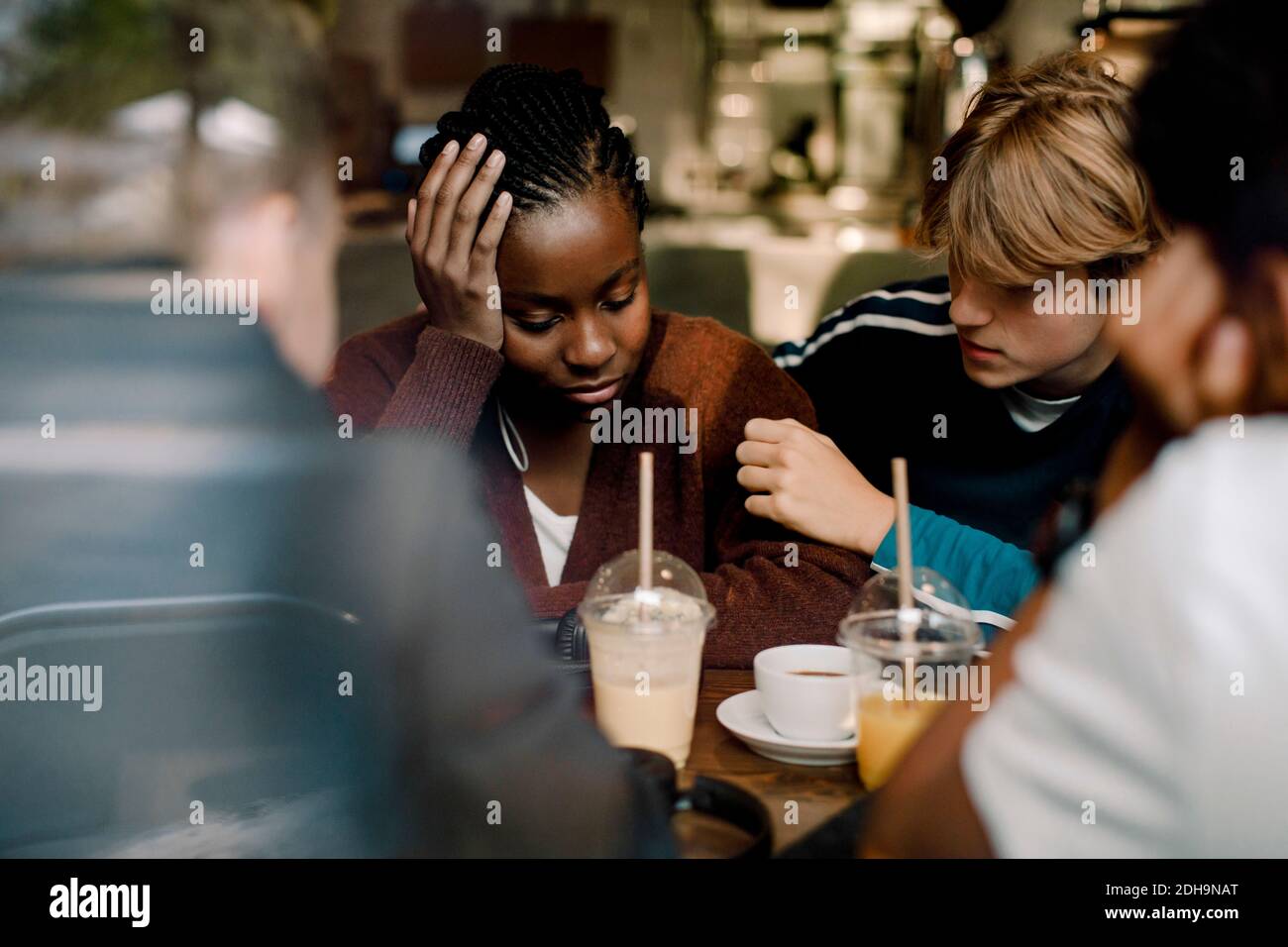 Teenage boy consoling female friend while sitting at cafe seen through ...