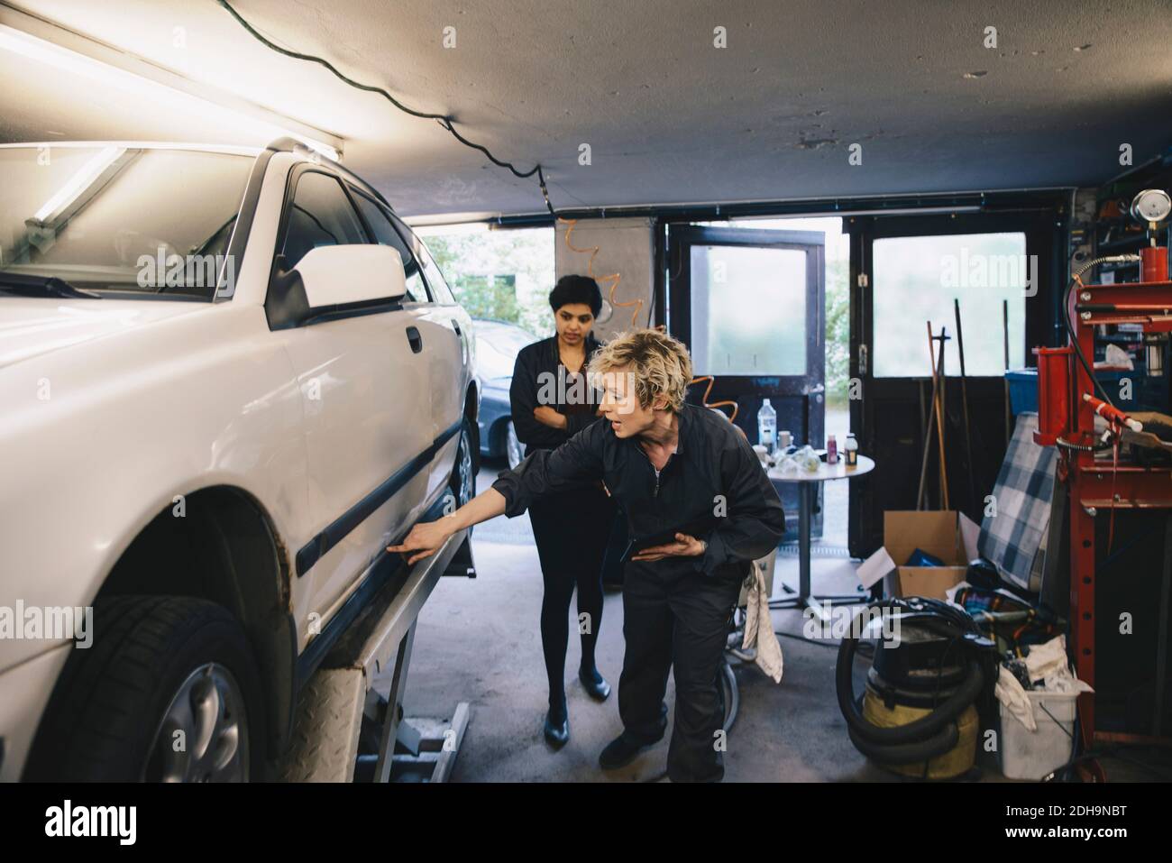 Female mechanic pointing while showing car to customer in auto repair ...