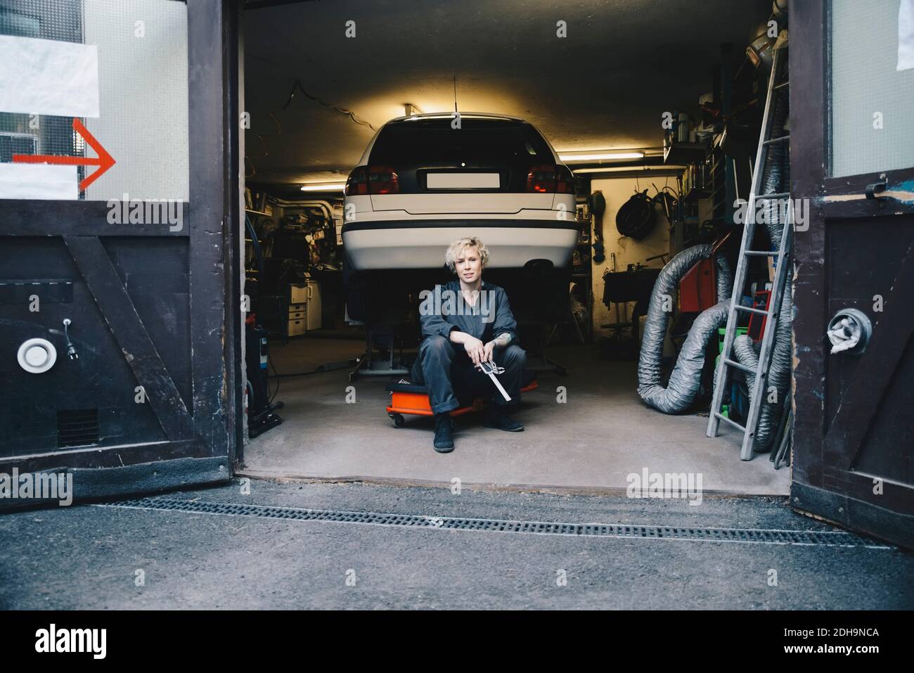 Female mechanic sitting by car at entrance of auto repair shop Stock ...