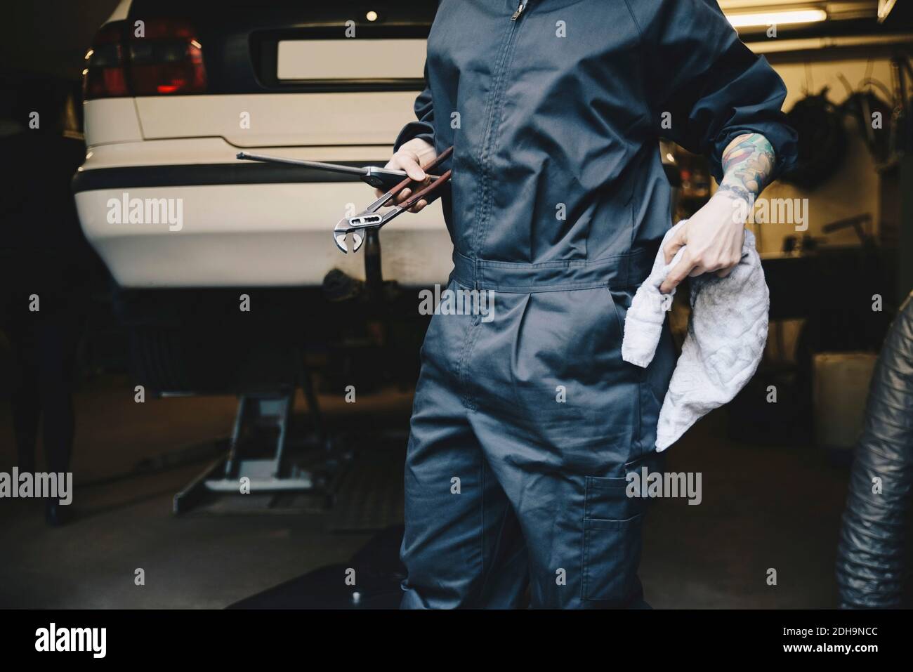 Midsection of female mechanic holding napkin and work tools at auto ...