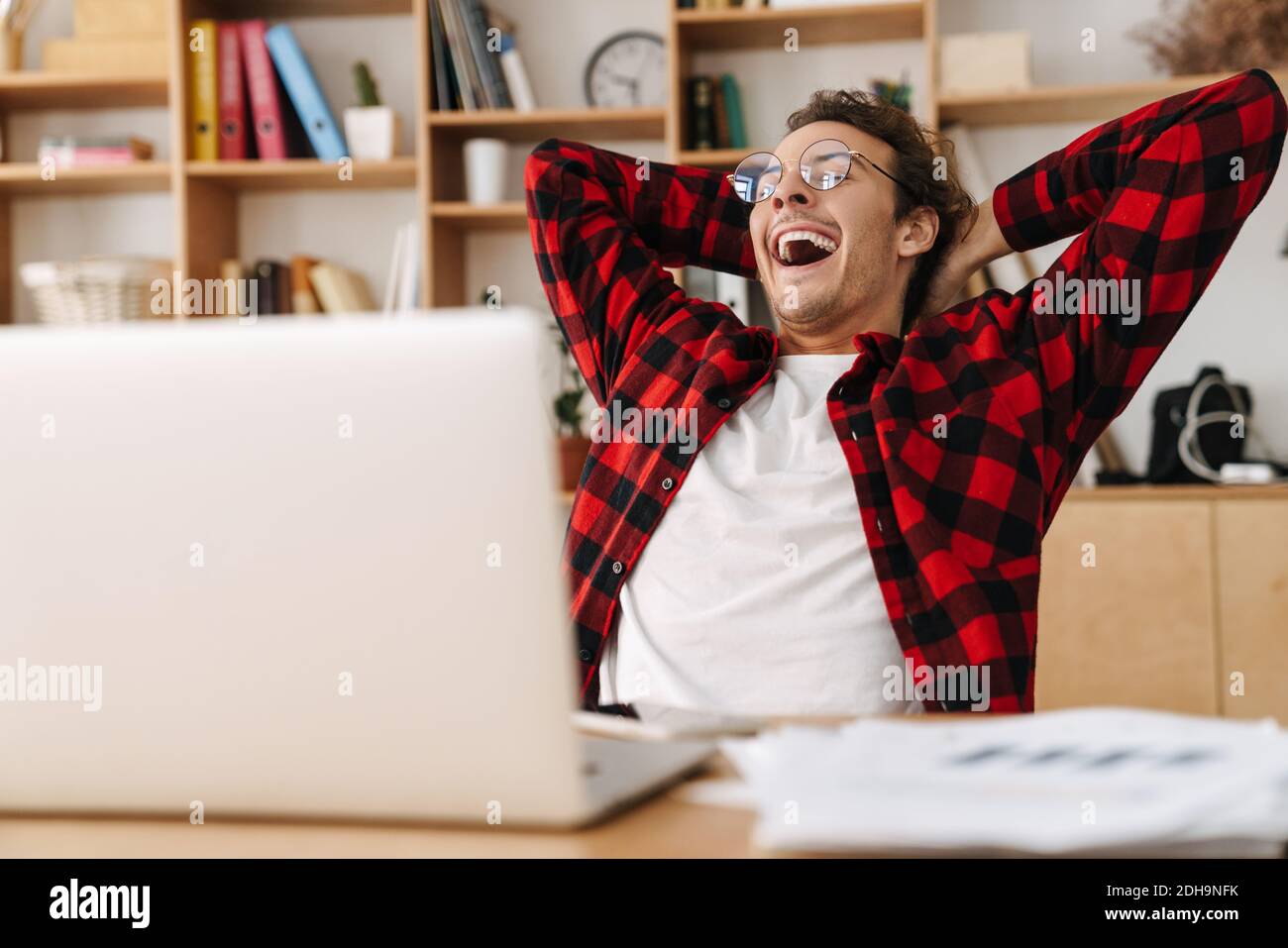 Handsome pleased guy in eyeglasses yawning while working with laptop at ...