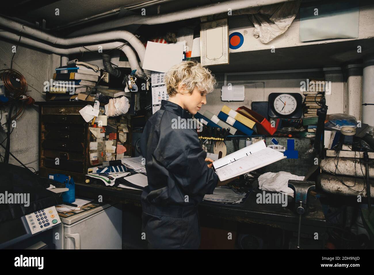 Side view of female mechanic reading document while standing in auto ...
