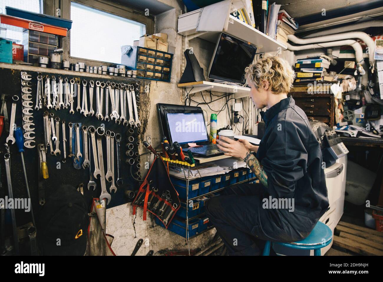 Side view of female mechanic holding disposable cup while using laptop ...