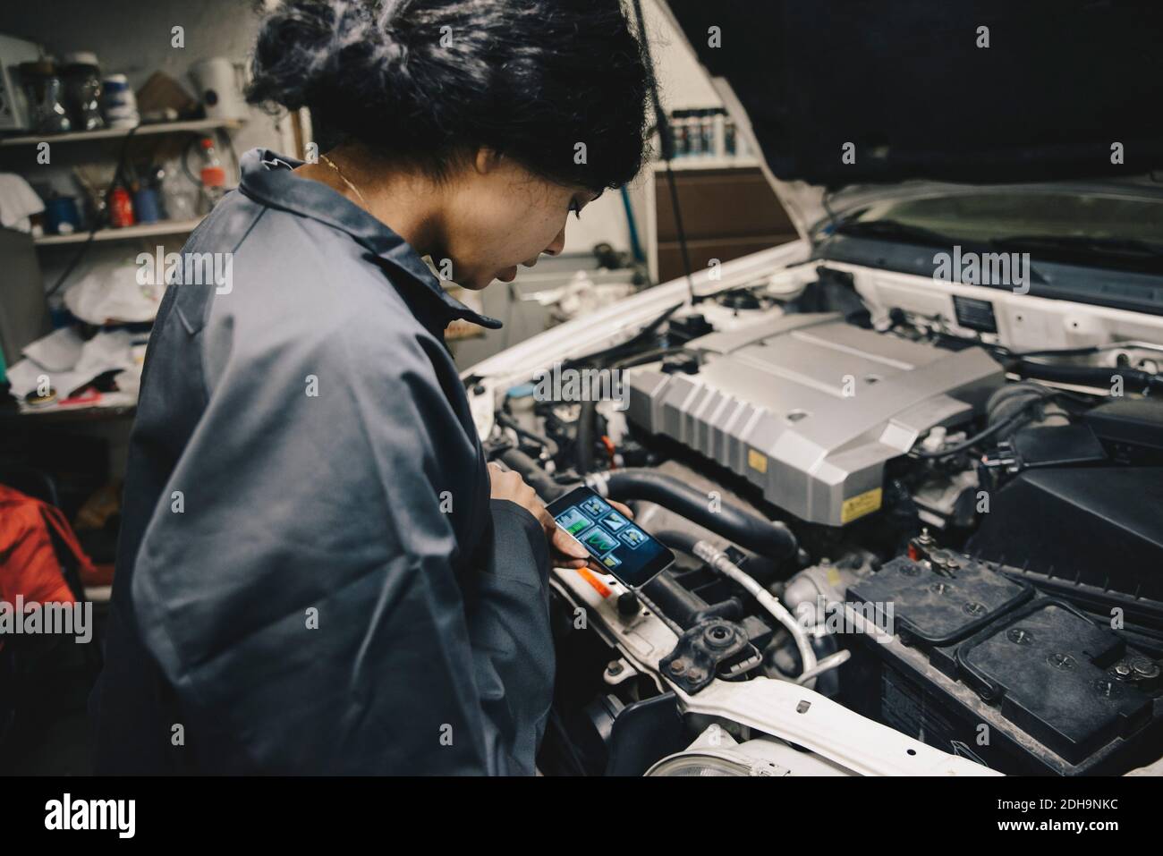 Female mechanic using application on smart phone while standing by open ...