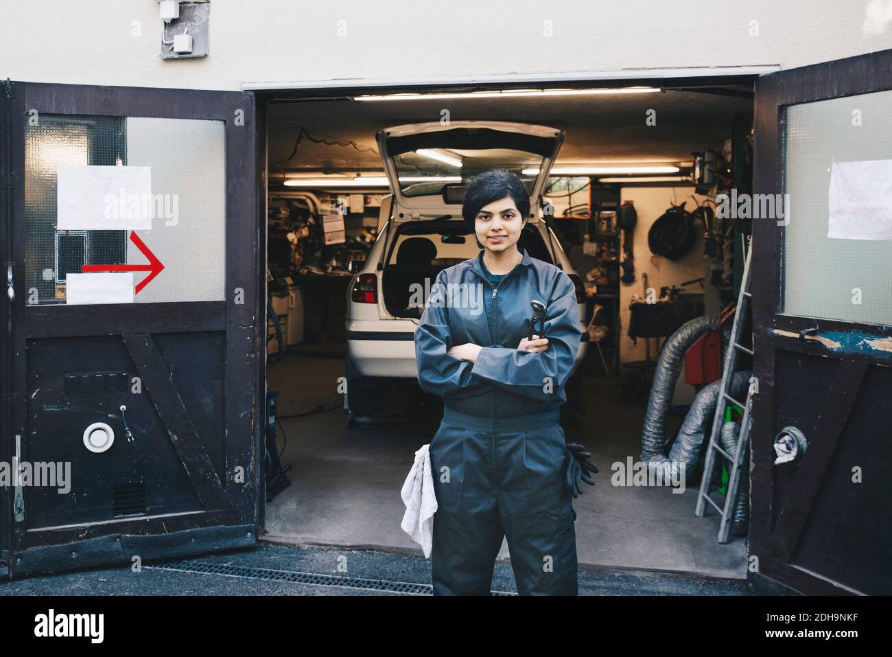 Portrait of confident female mechanic standing at entrance of auto ...