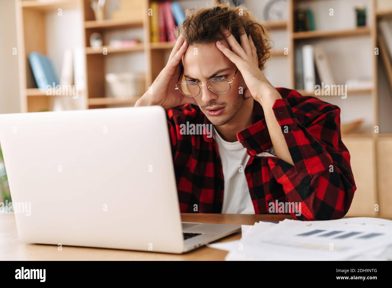 Handsome brooding guy in eyeglasses working with laptop while sitting ...