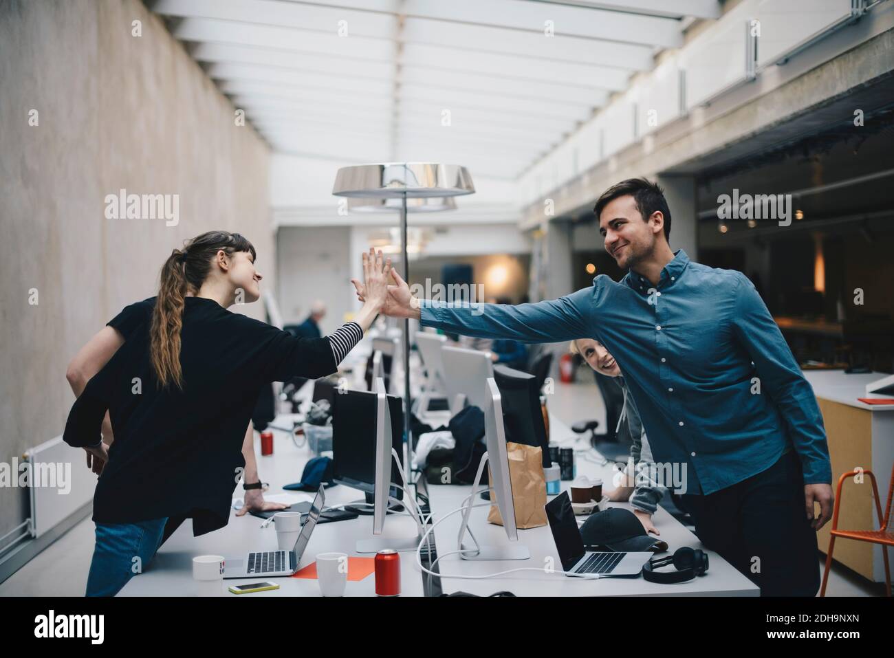 Male and female computer programmers giving high-five over desk in ...