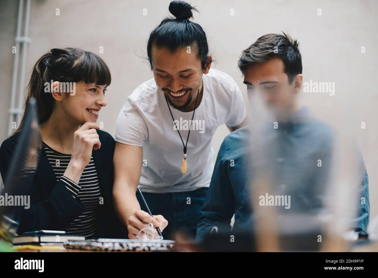 Happy computer programmer writing while discussing with colleagues in ...