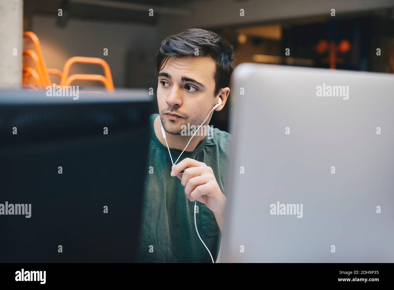 Thoughtful computer programmer wearing in-ear headphones in office ...