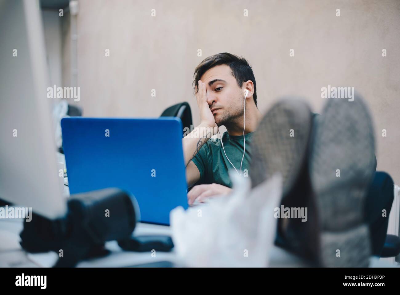 Tired computer programmer using laptop while sitting with feet up at ...