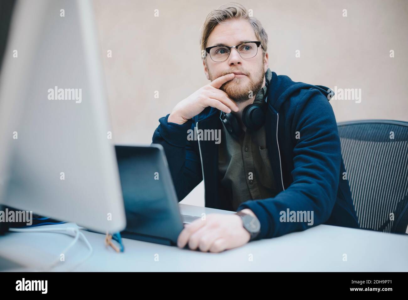Thoughtful computer programmer sitting at desk in office Stock Photo ...