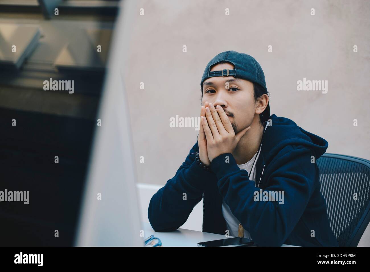 Male computer programmer sitting with hands covering mouth at computer ...