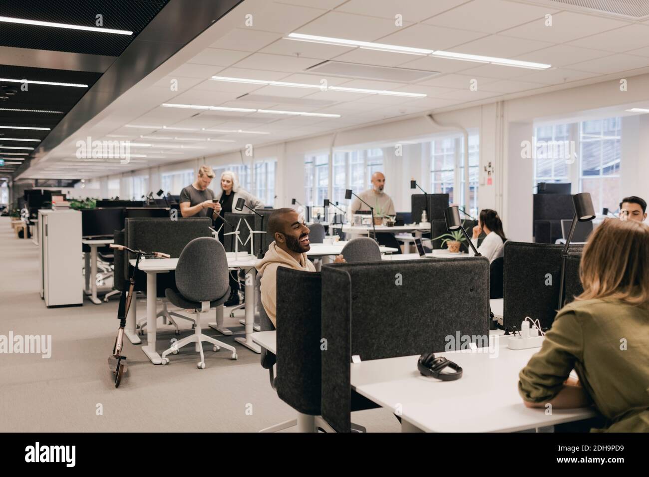 Male and female colleagues talking while working at desk in creative ...