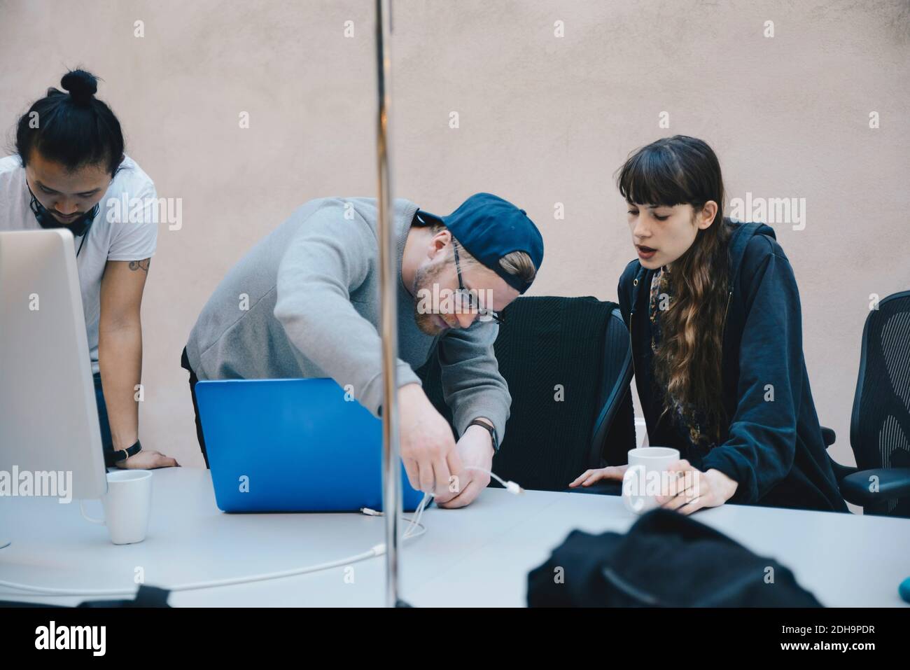 Computer programmer connecting cable laptop while colleagues at desk in ...