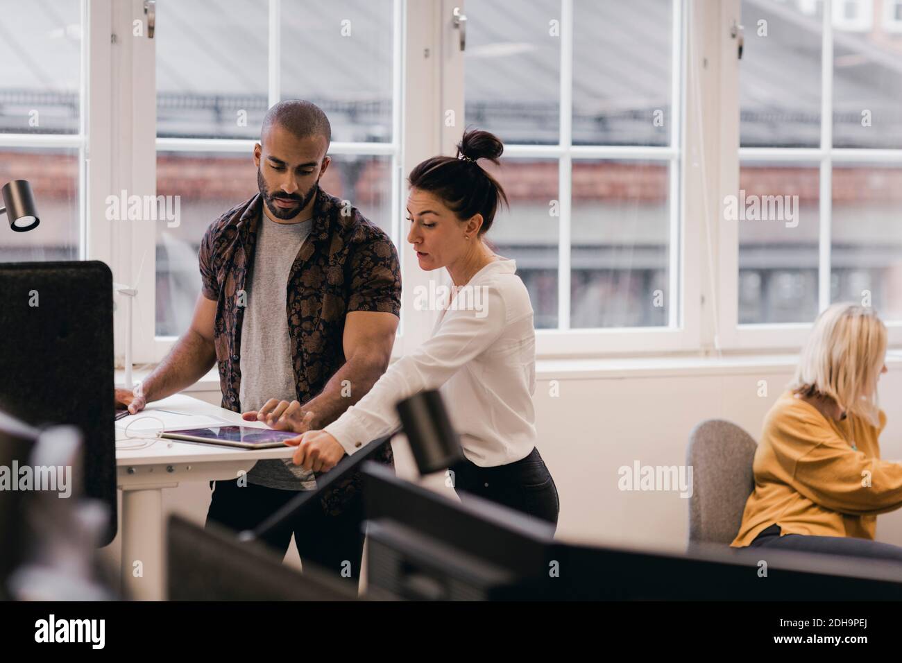 Businesswoman discussing with male coworker over digital tablet at ...