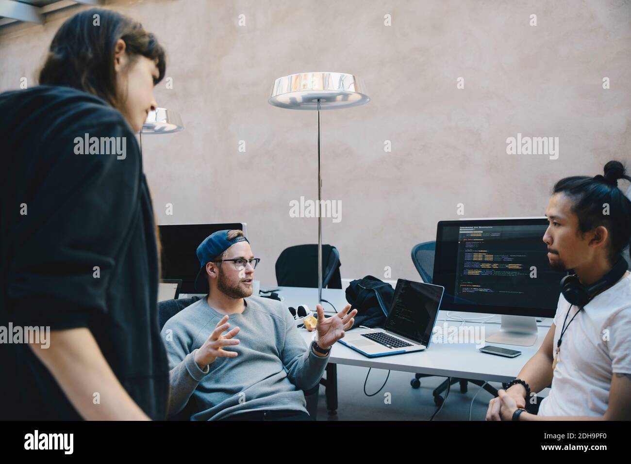 Computer programmer gesturing while discussing plan with colleagues in ...