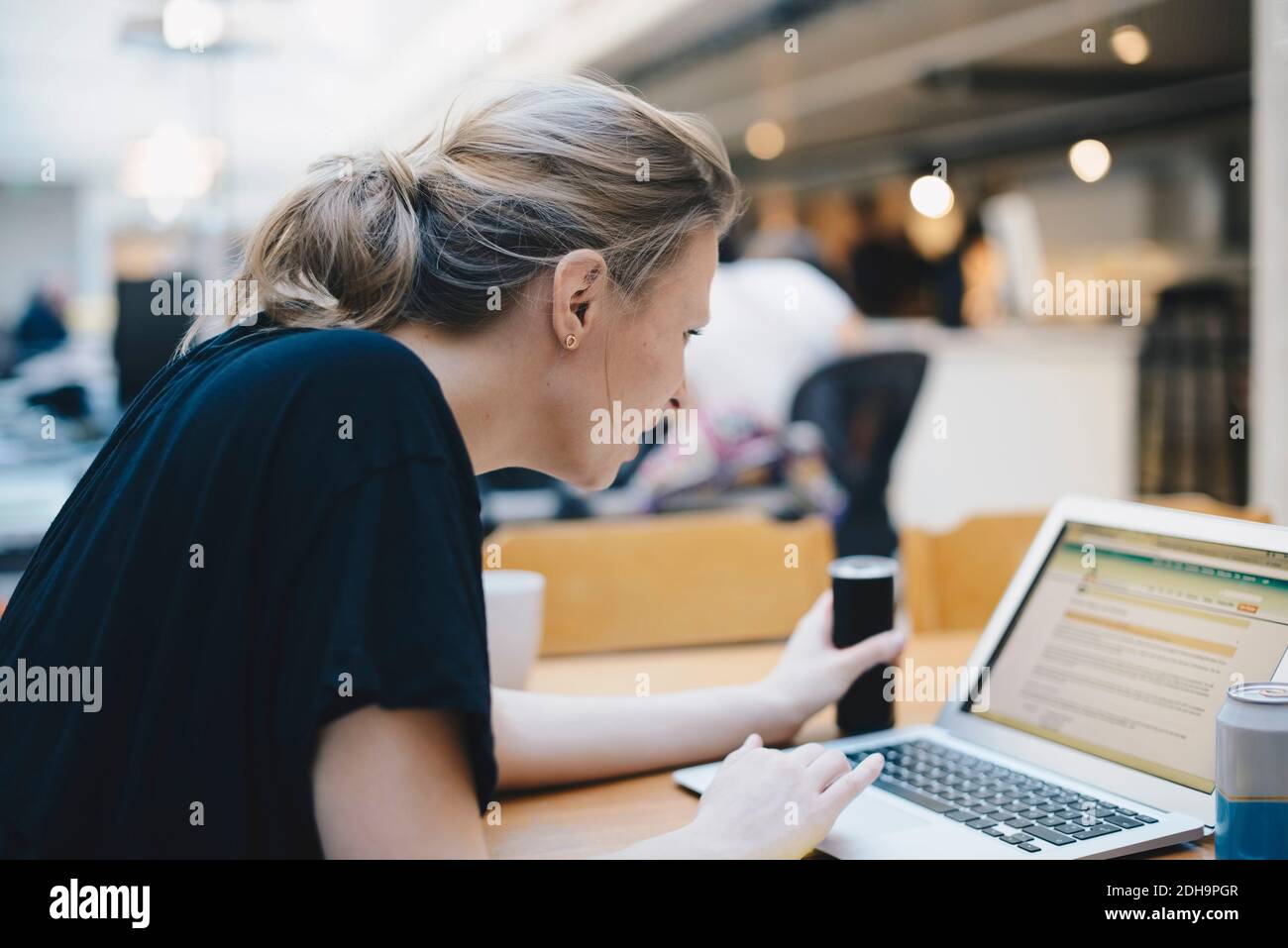 Side view of young female computer programmer using laptop at desk in ...