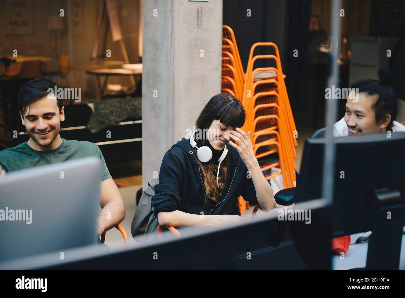 Happy female computer programmer sitting with male colleagues in office ...