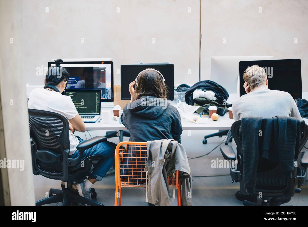 Rear view of programmers using computers at desk in office Stock Photo ...