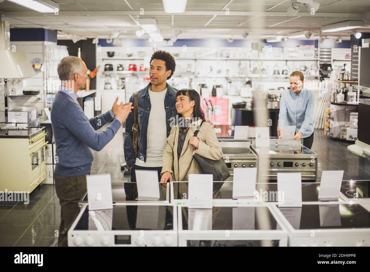 Mature owner talking to smiling female and male customers in ...