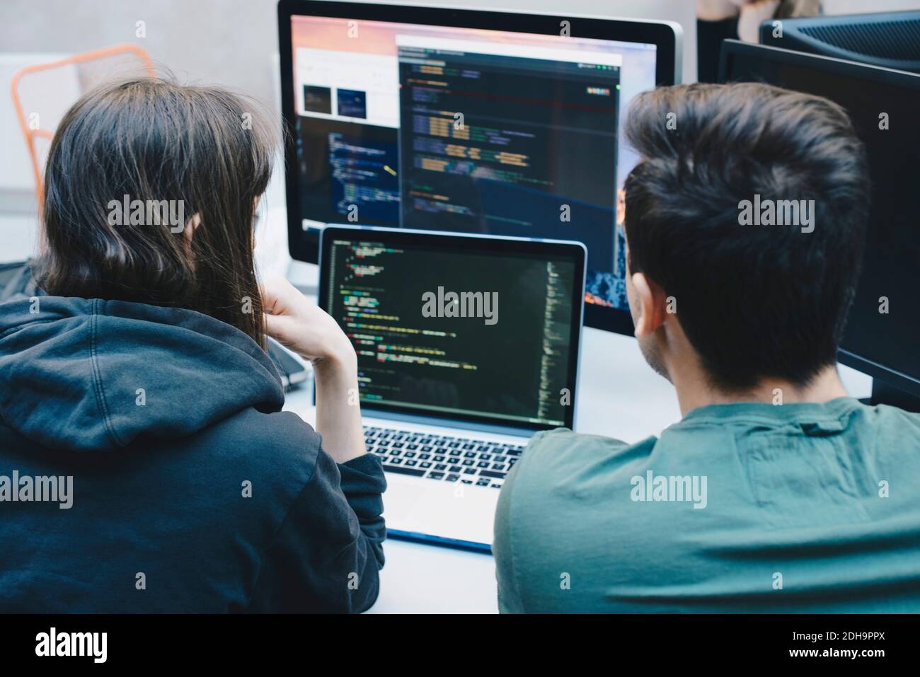 Rear view of computer programmers using laptop at office desk Stock ...