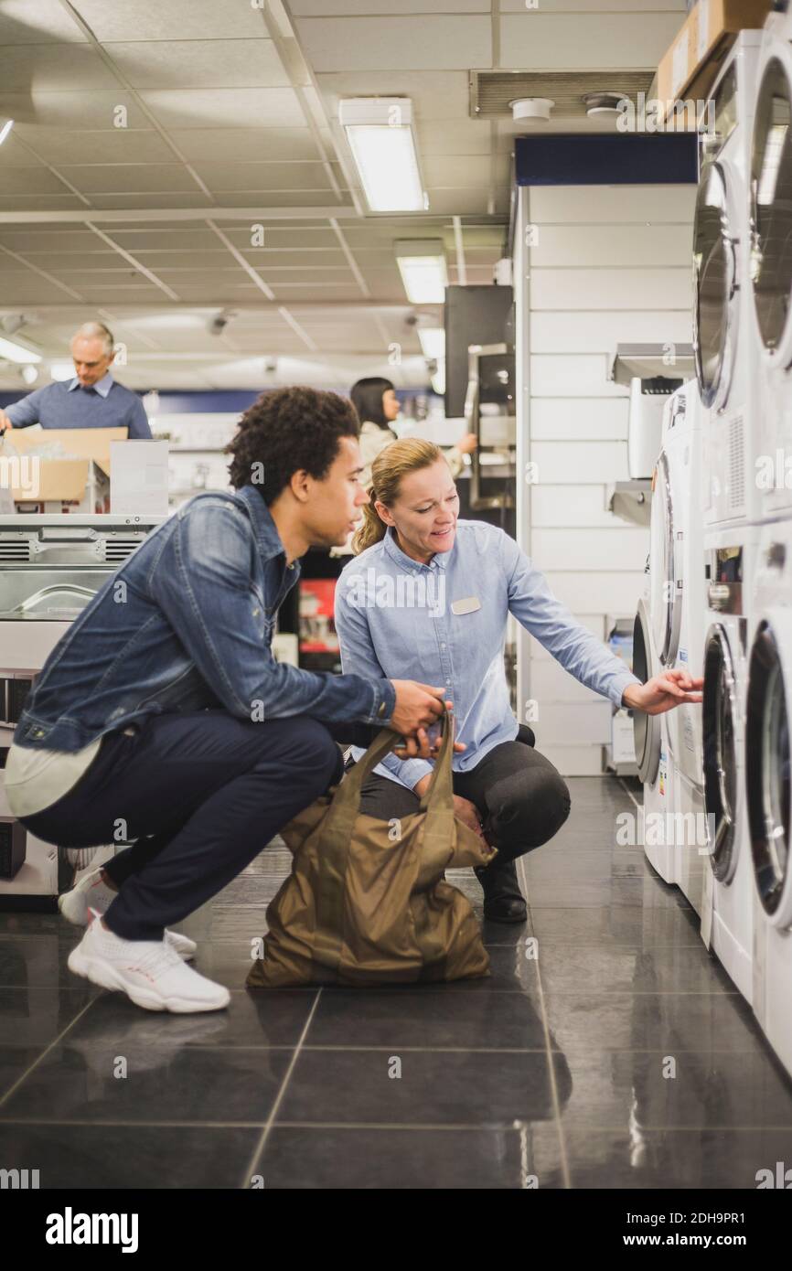 Mature owner explaining about washing machine to male customer in ...