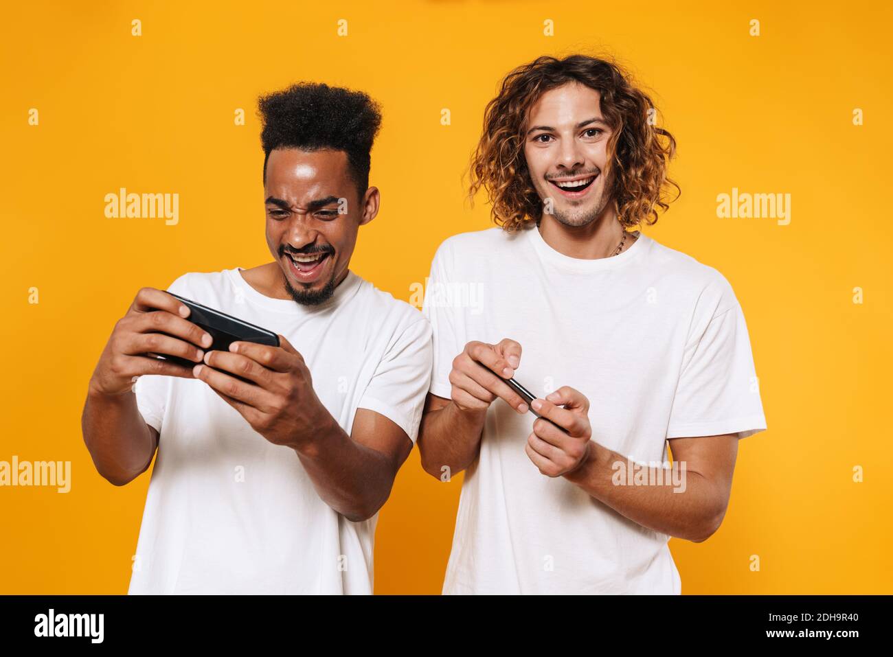 Excited multicultural two guys playing online games on smartphones ...