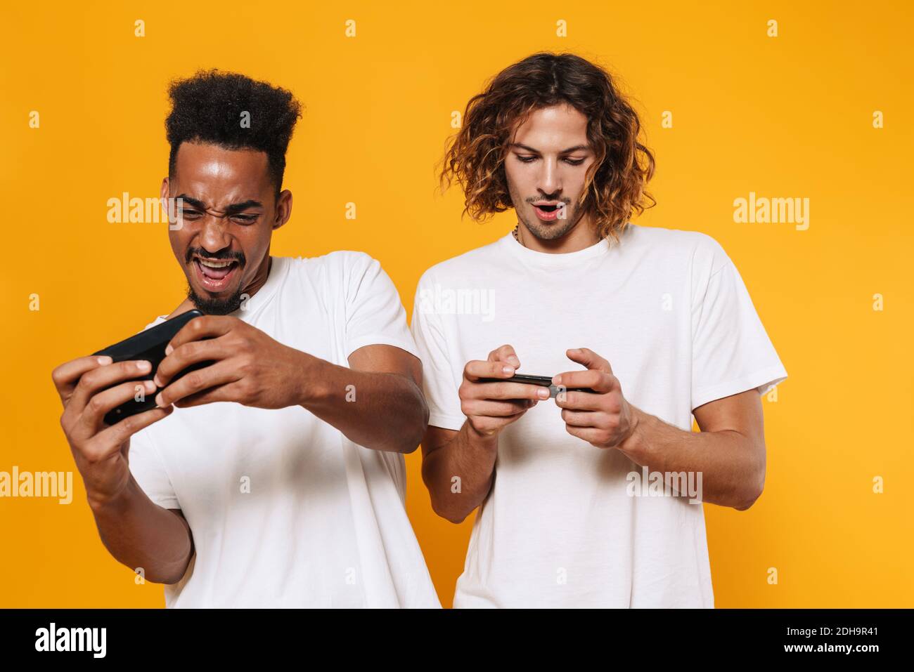 Excited multicultural two guys playing online games on smartphones ...