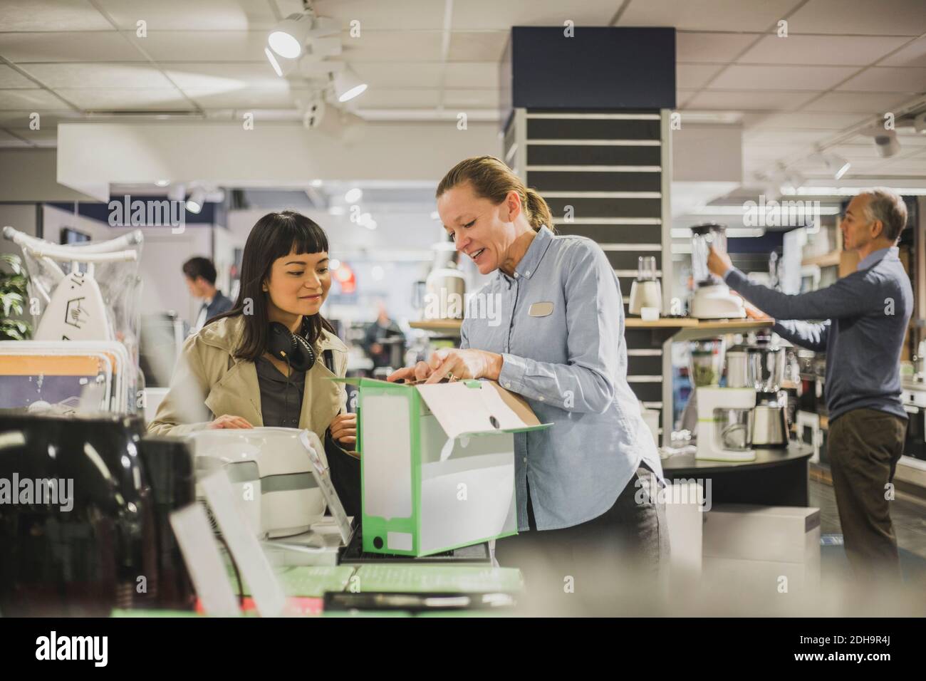 Mature female owner showing appliance to young customer in electronics ...