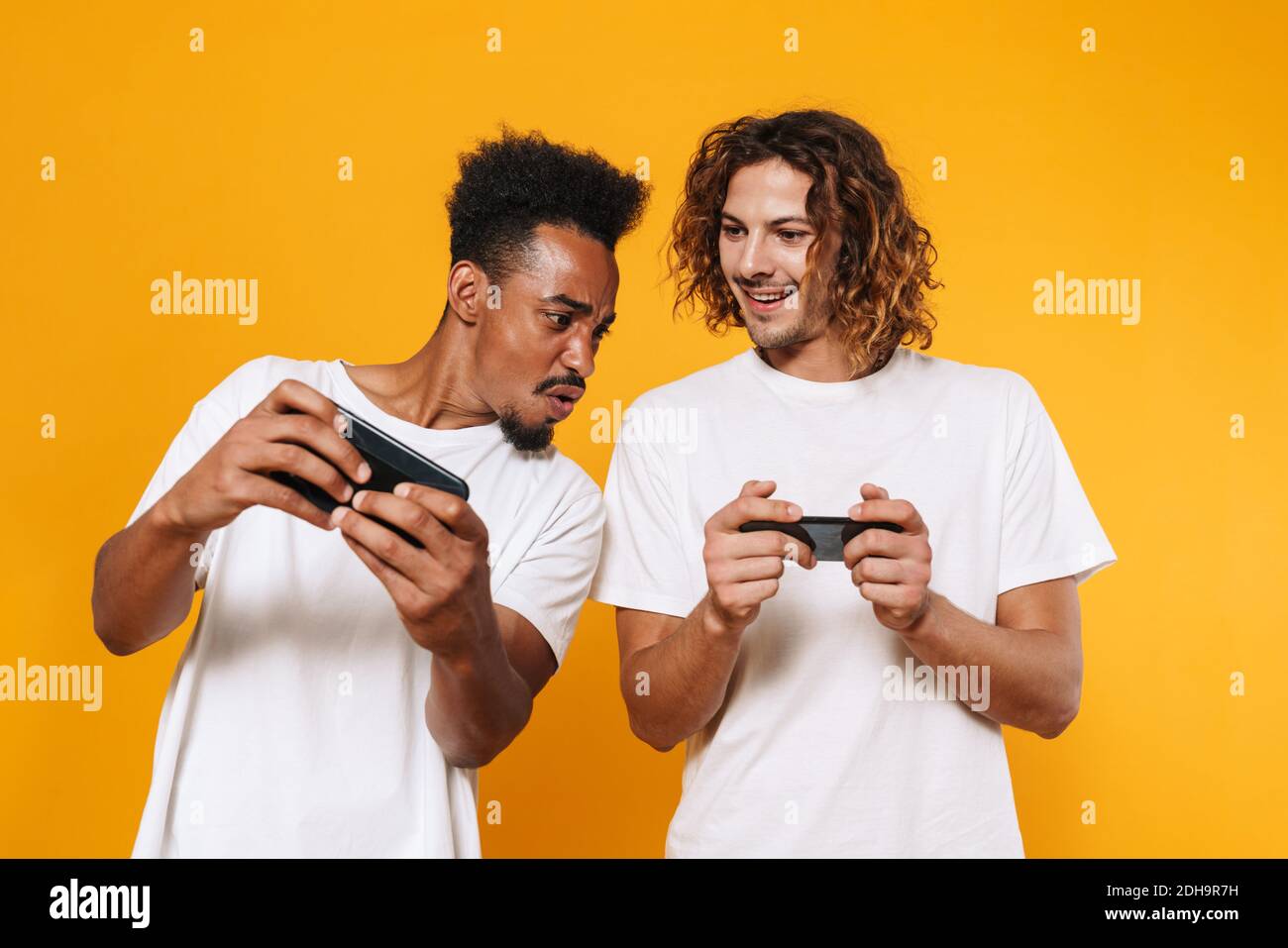 Focused multicultural two guys playing online games on smartphones ...