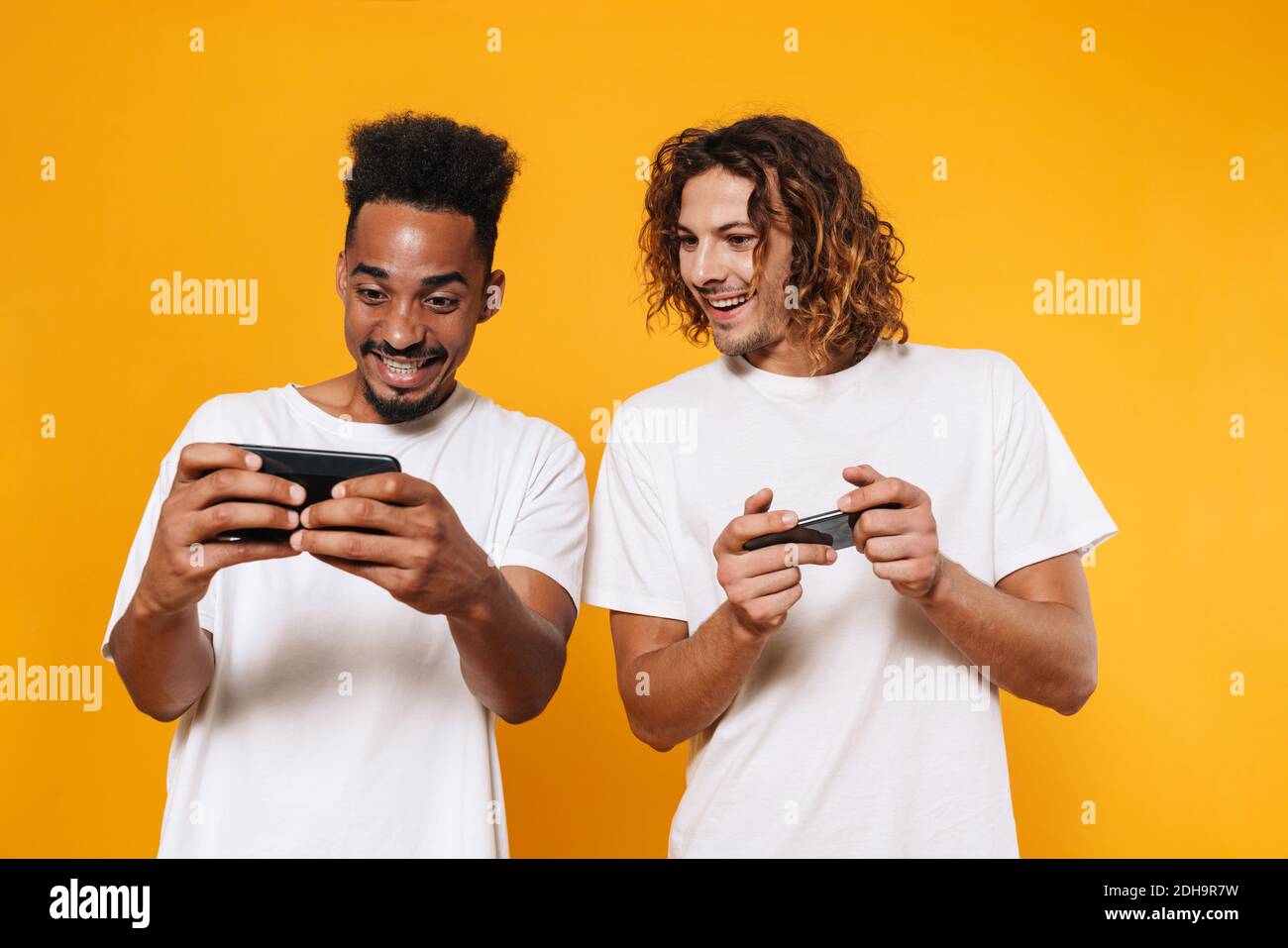 Smiling multicultural two guys playing online games on smartphones ...