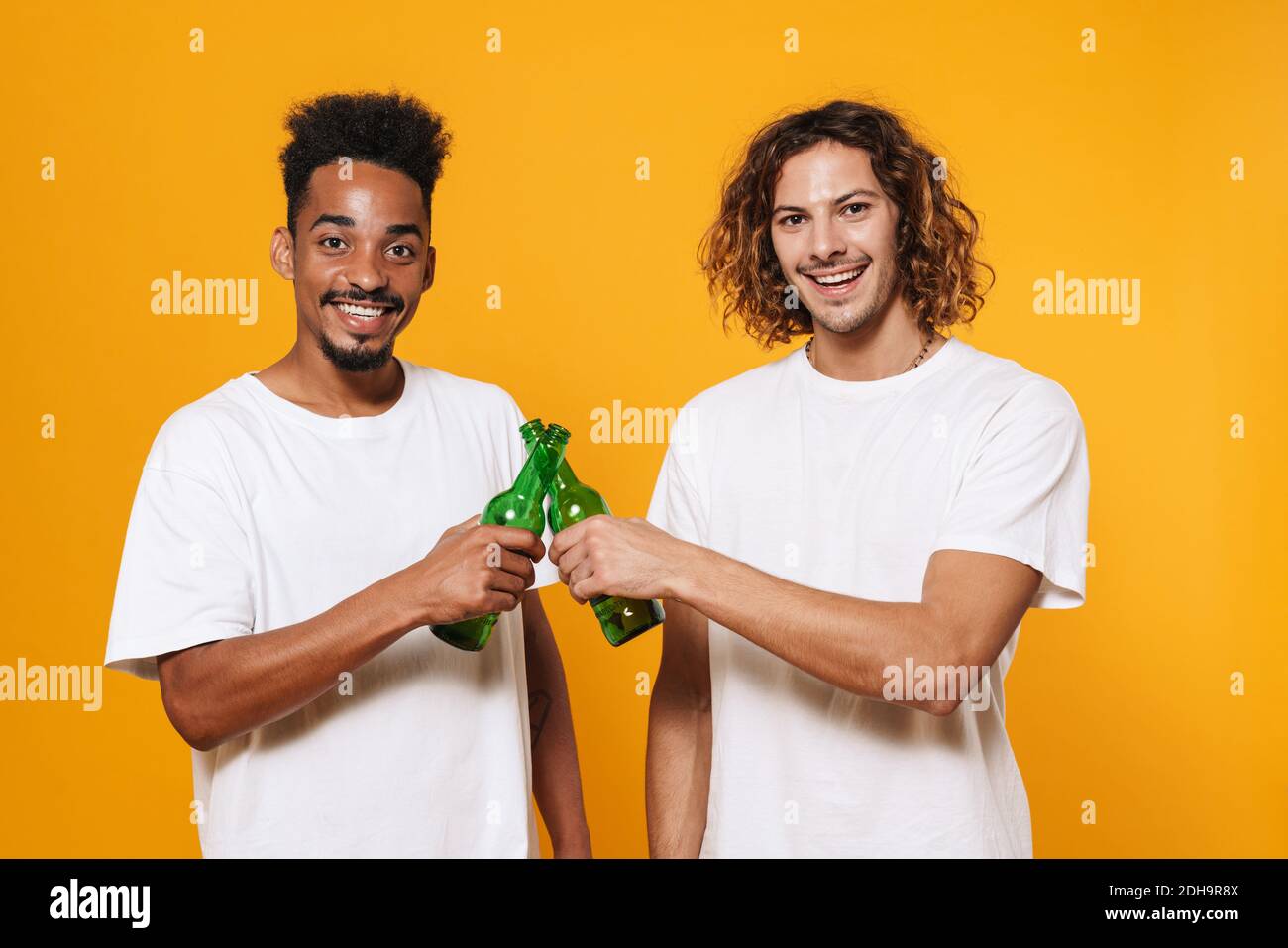 Happy multicultural two guys smiling and clinking bottles isolated over ...