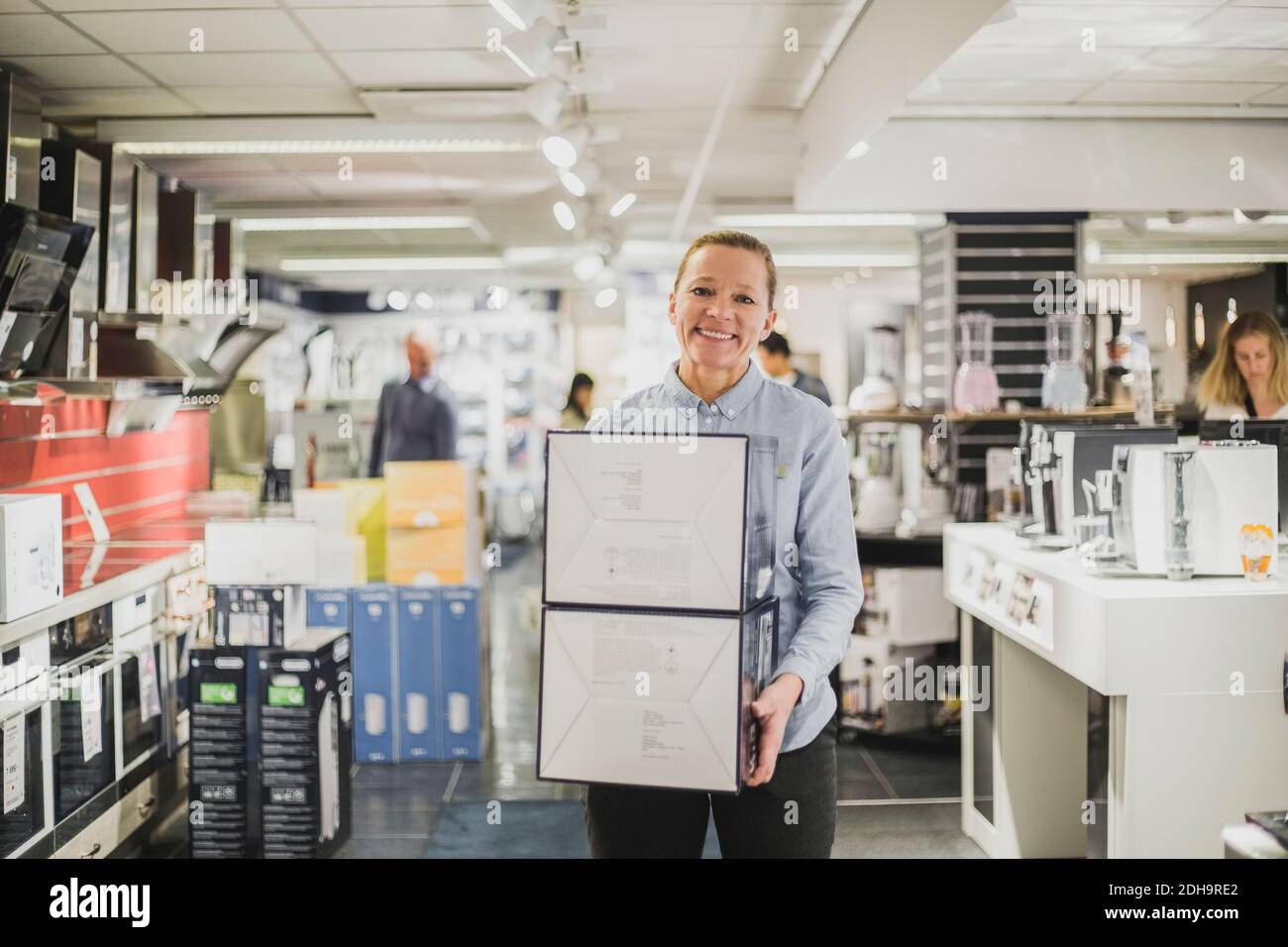 Portrait of smiling mature female owner with boxes standing in ...