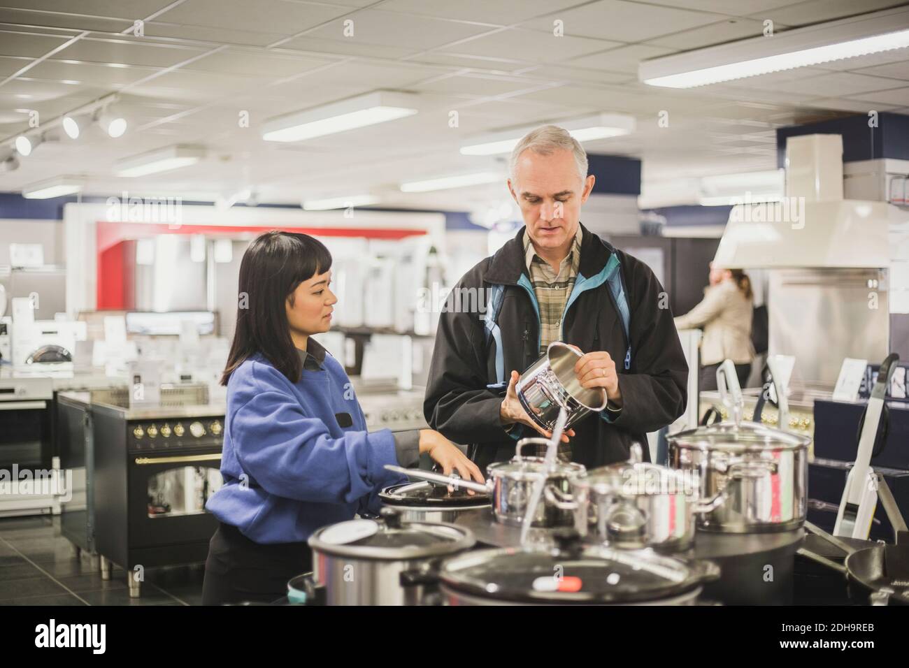 Young owner showing kitchen utensil to mature customer in store Stock ...